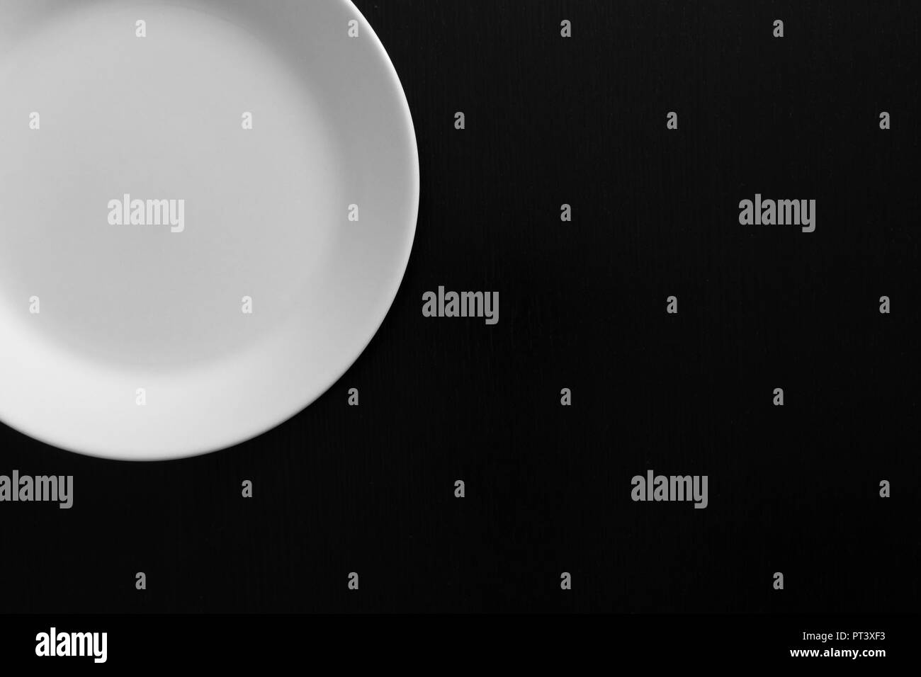 Empty white plate on black wooden table. Kitchen tools close up Stock ...