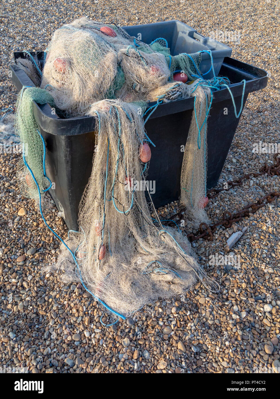 Nylon fishing nets spilling from a grey plastic container on a pebble ...