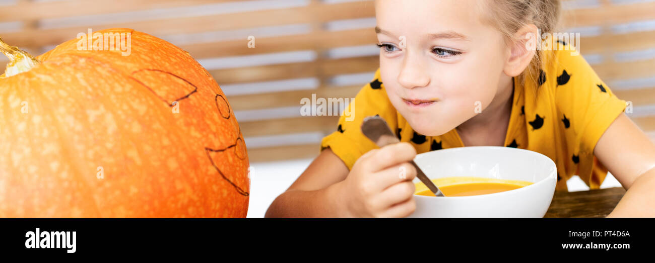 Cute little girl eating pumpkin soup and looking at a large Halloween ...