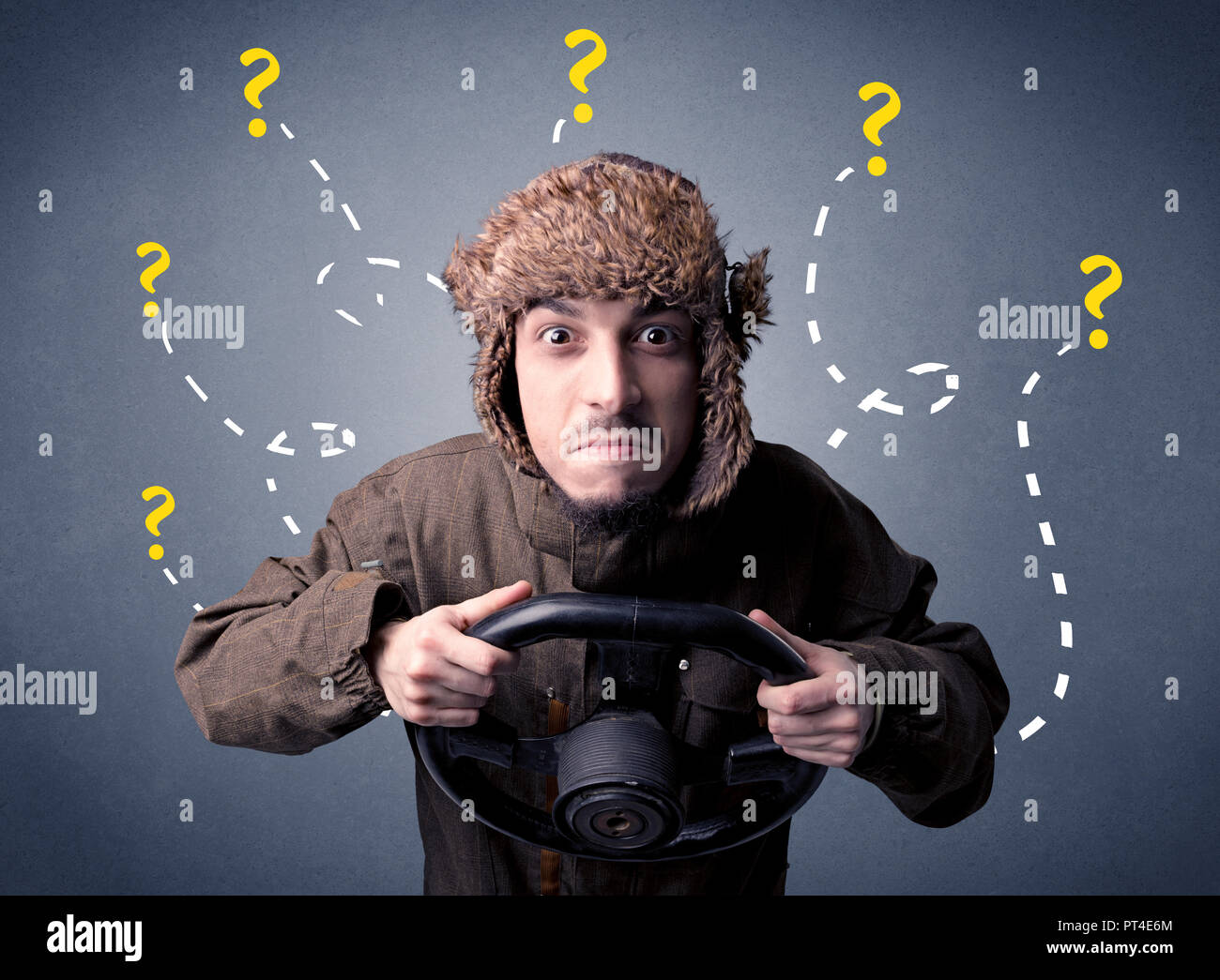 Young man holding black steering wheel with question marks around him ...
