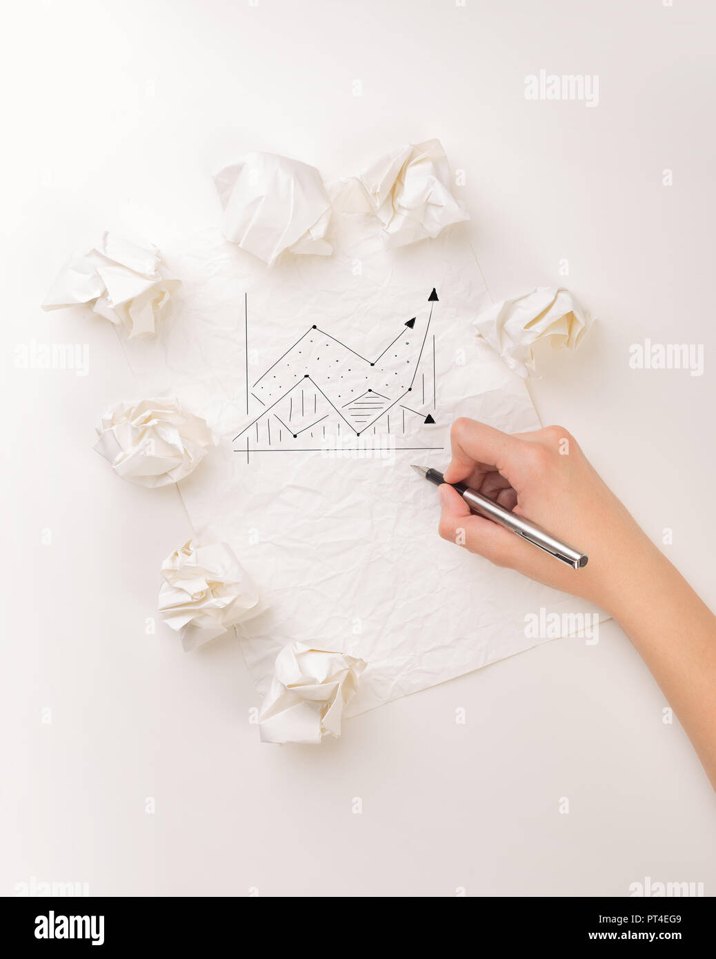 Female hand next to a few crumpled paper balls drawing a progress chart ...