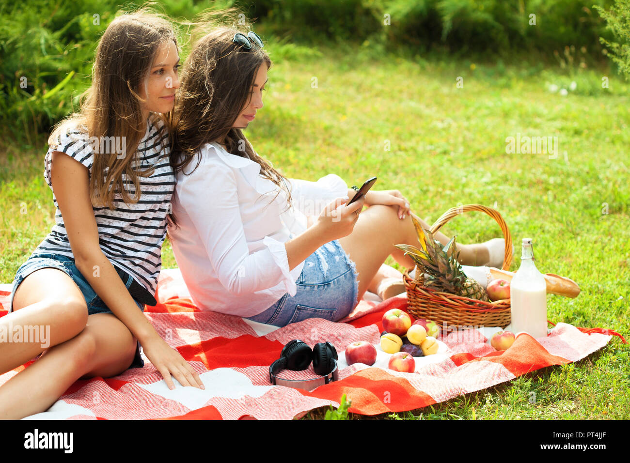 Two beautiful young women on a picnic looking at the smartphone screen . Summer time Stock Photo ...