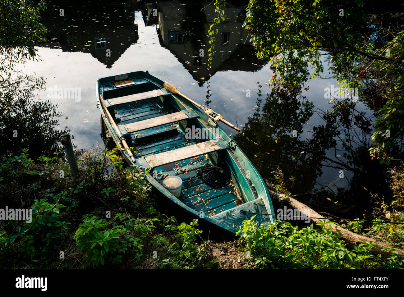 single green boat with leaves and house reflections Stock Photo - Alamy