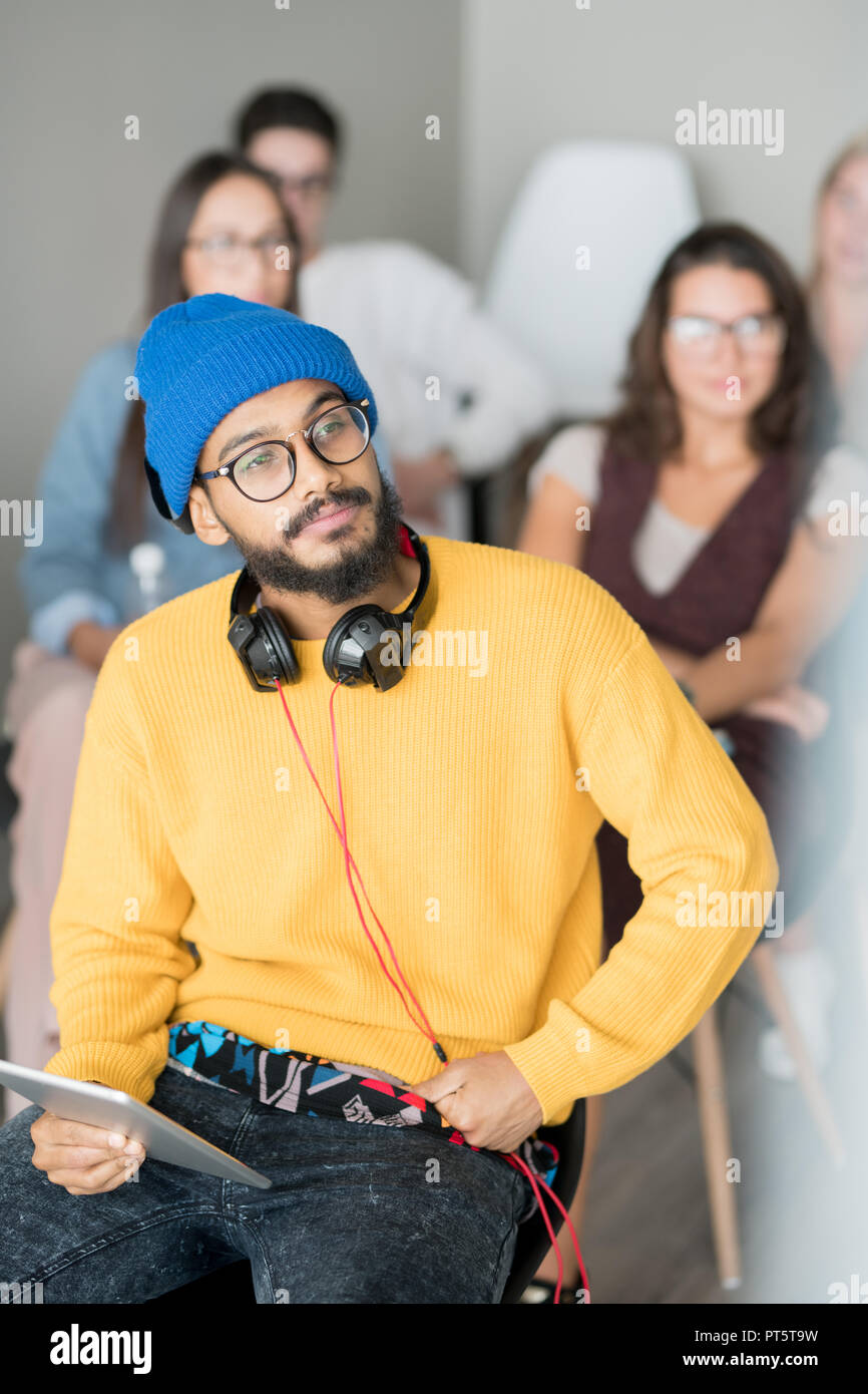 Serious pensive young Arabian student with beard wearing bright hat and ...
