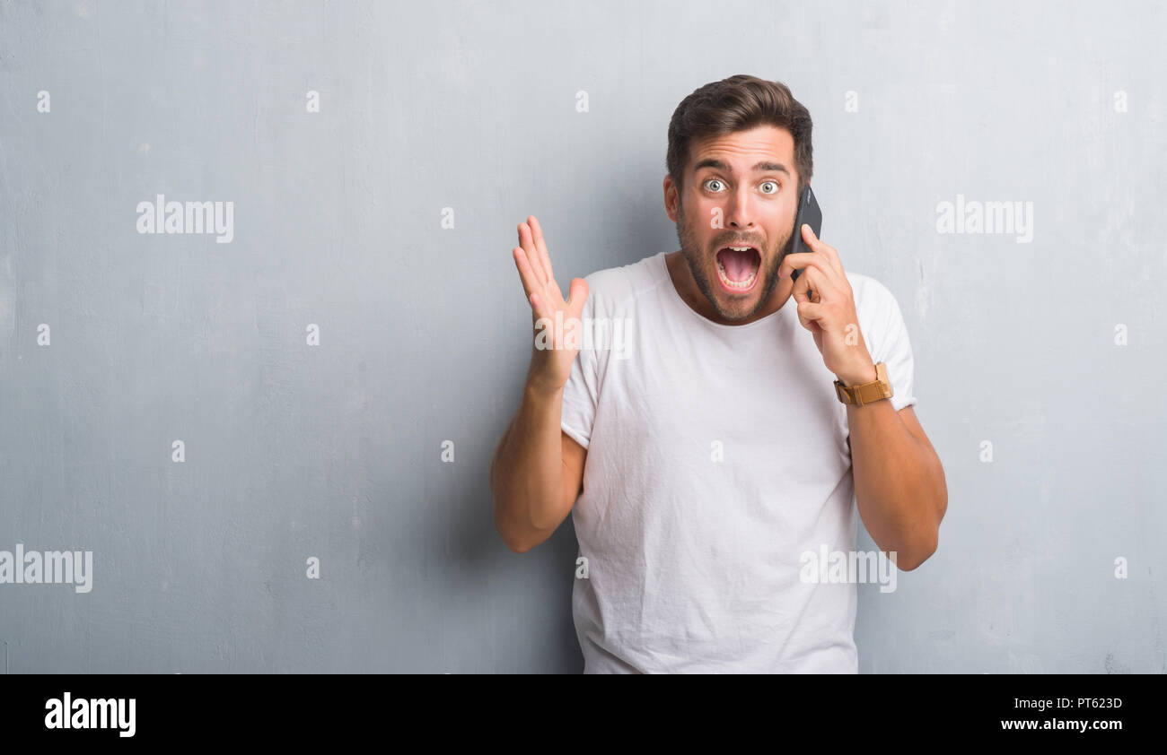 Handsome young man over grey grunge wall speaking on the phone very ...