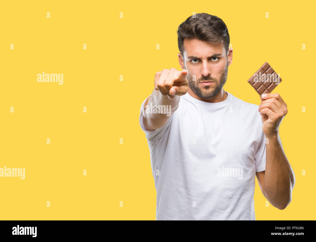 Young handsome man eating chocolate bar over isolated background ...