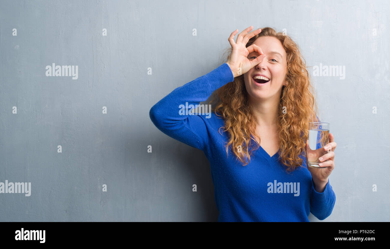 Young redhead woman over grey grunge wall drinking water with happy ...