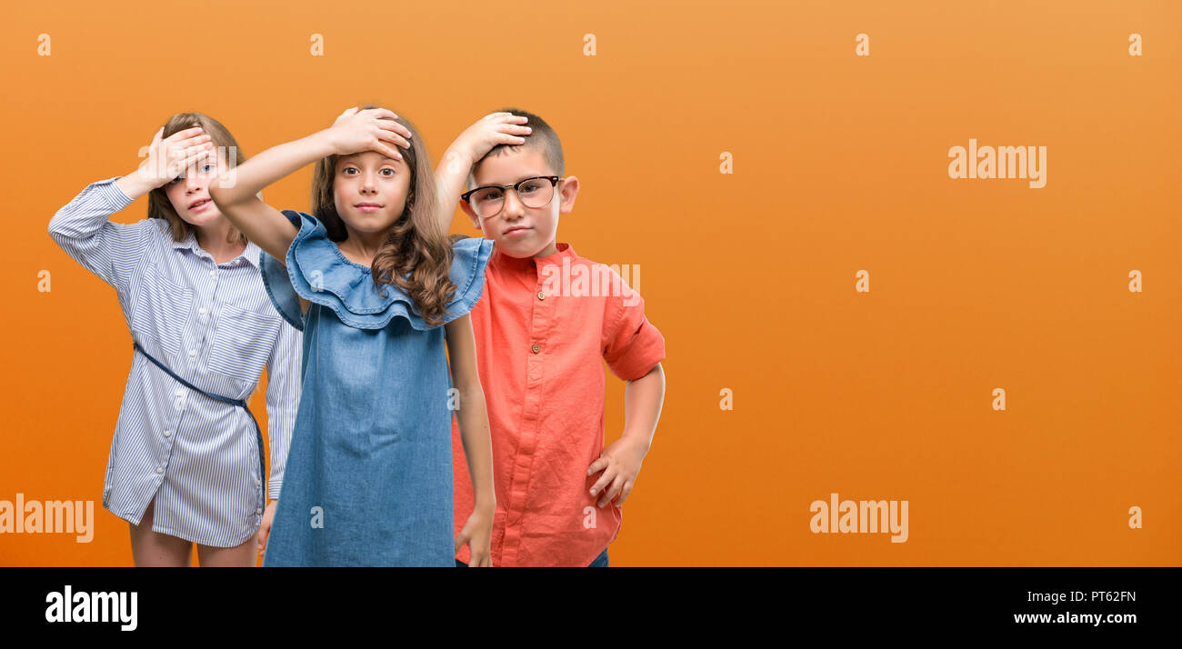 Group of boy and girls kids over orange background stressed with hand ...