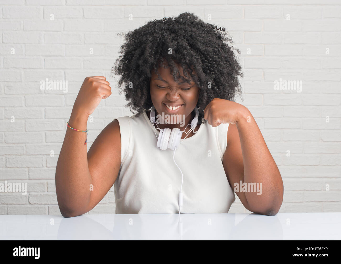 Young african american woman sitting on the table wearing headphones ...