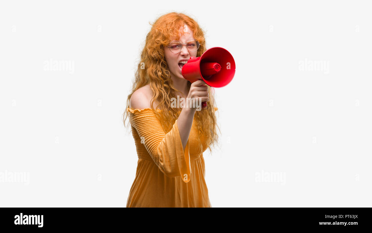Young redhead woman holding megaphone annoyed and frustrated shouting ...