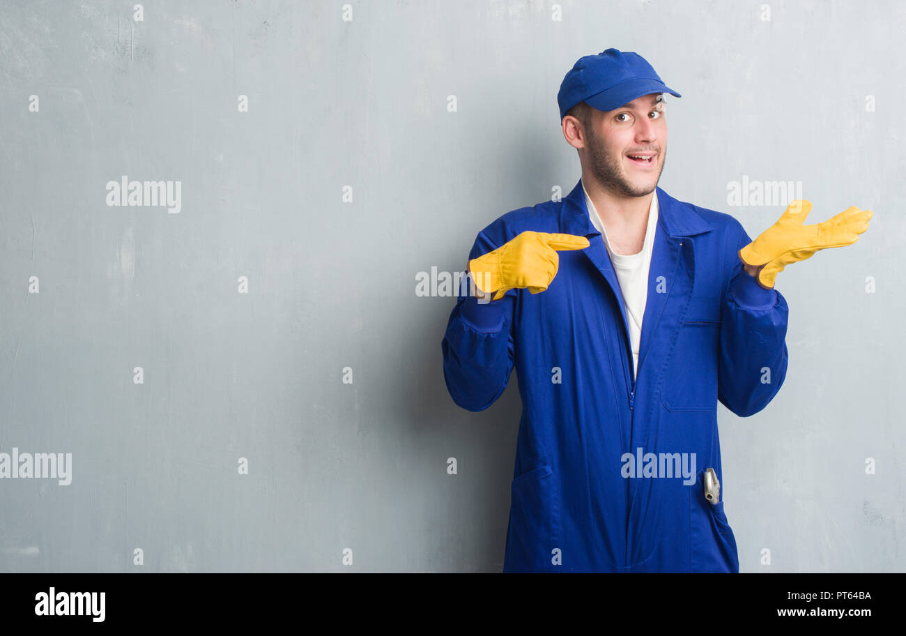 Young caucasian man over grey grunge wall wearing mechanic uniform very ...