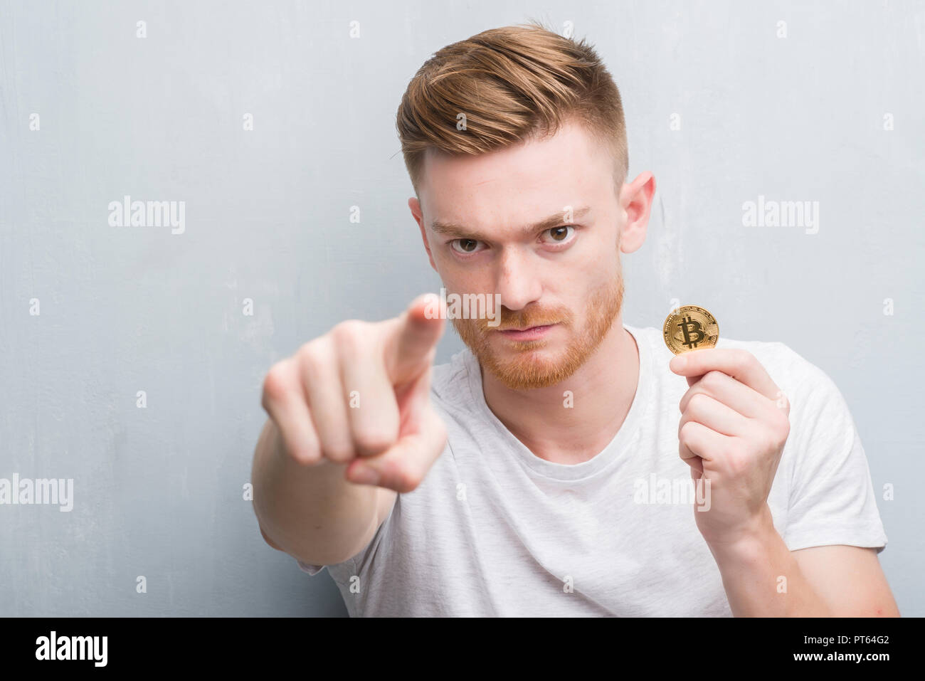 Young redhead man over grey grunge wall showing bitcoin pointing with ...