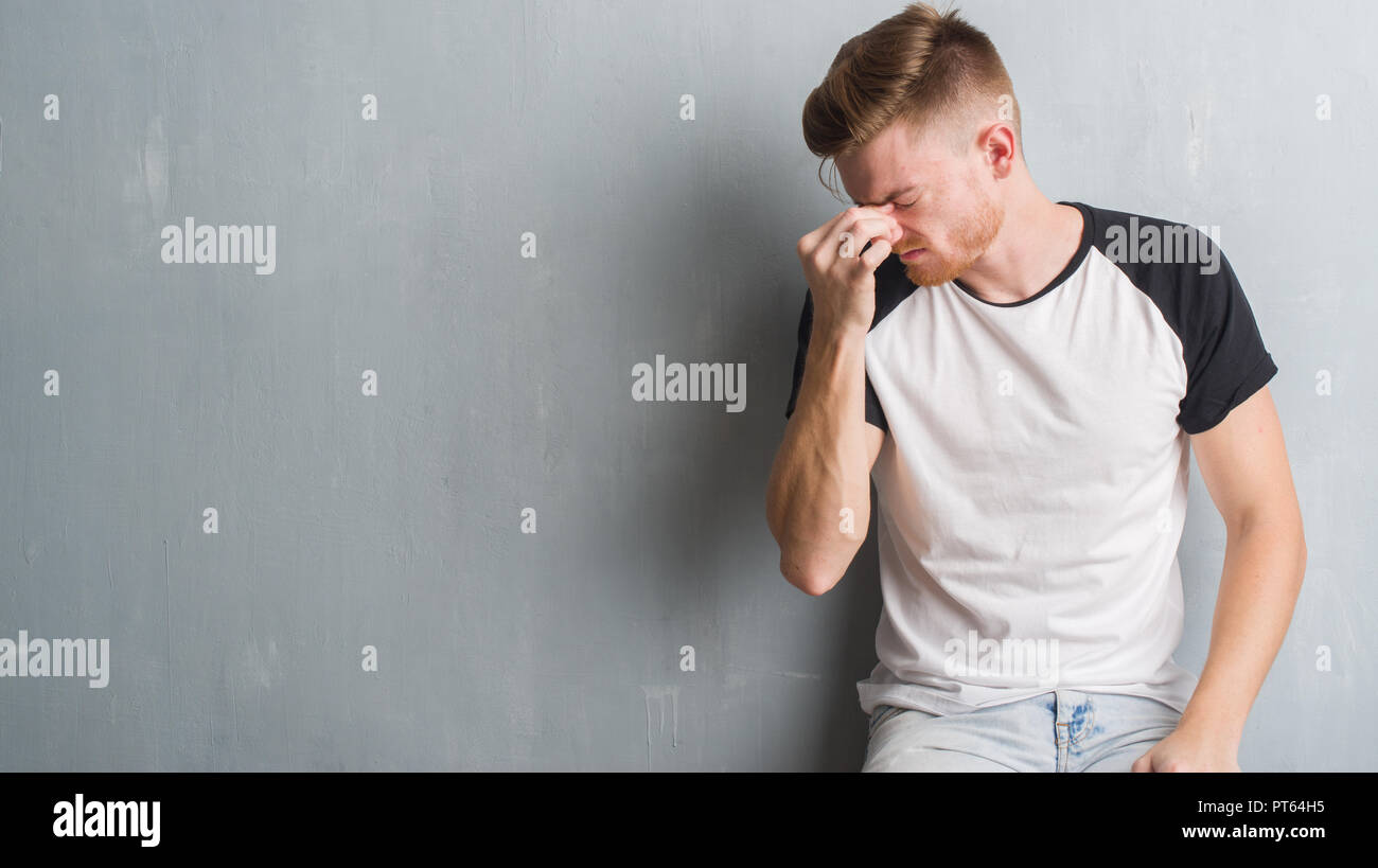 Young redhead man over grey grunge wall tired rubbing nose and eyes ...