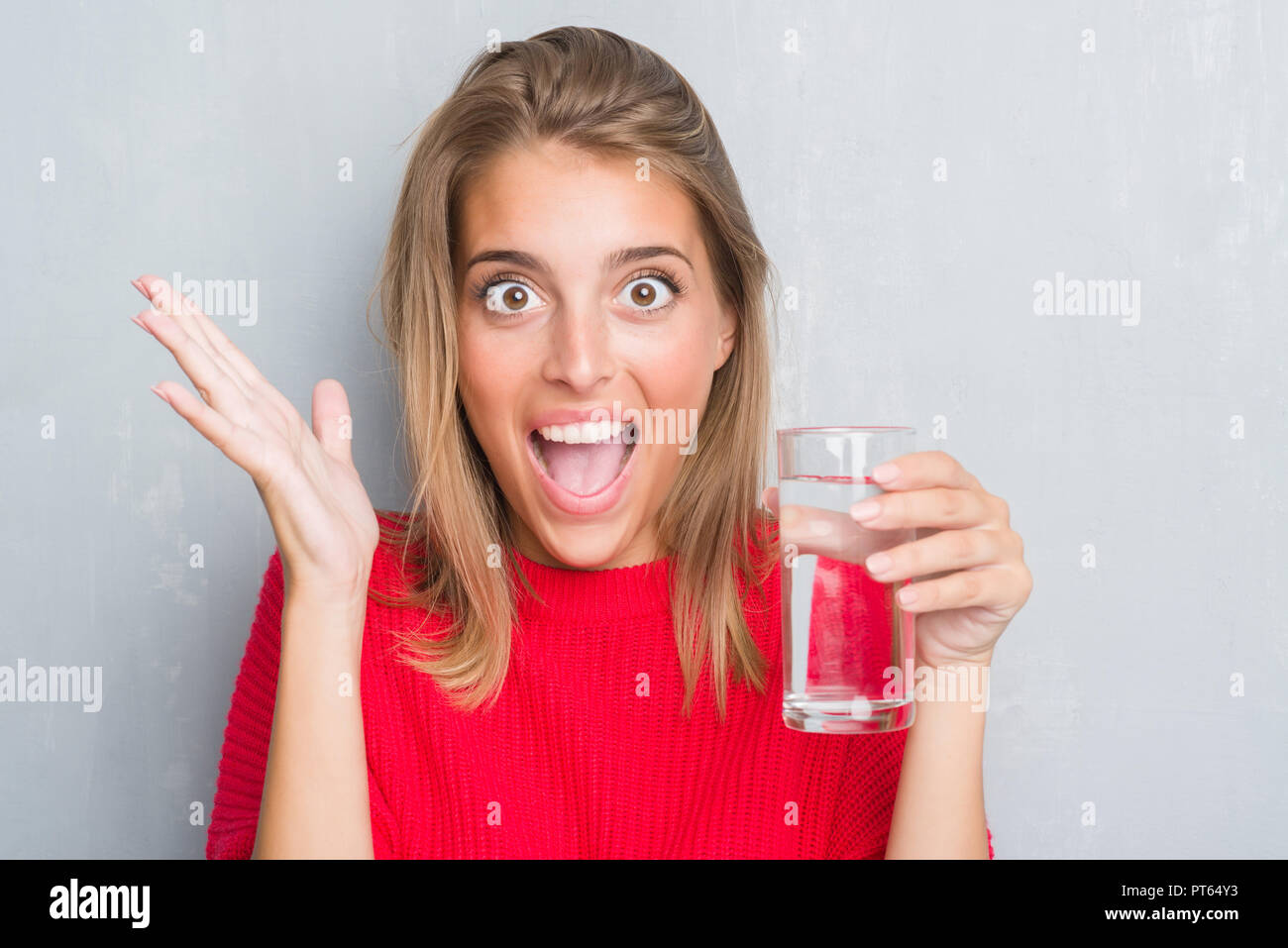 Beautiful young woman over grunge grey wall drinking a glass of water ...