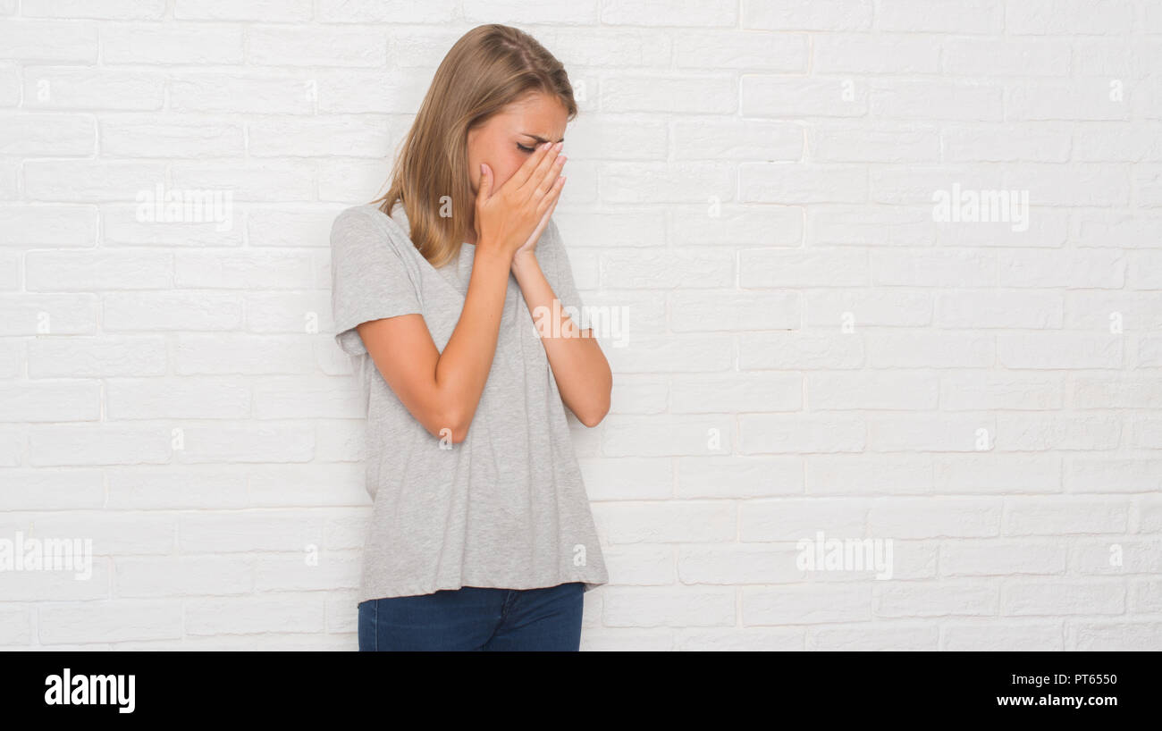 Beautiful young woman over white brick wall with sad expression ...