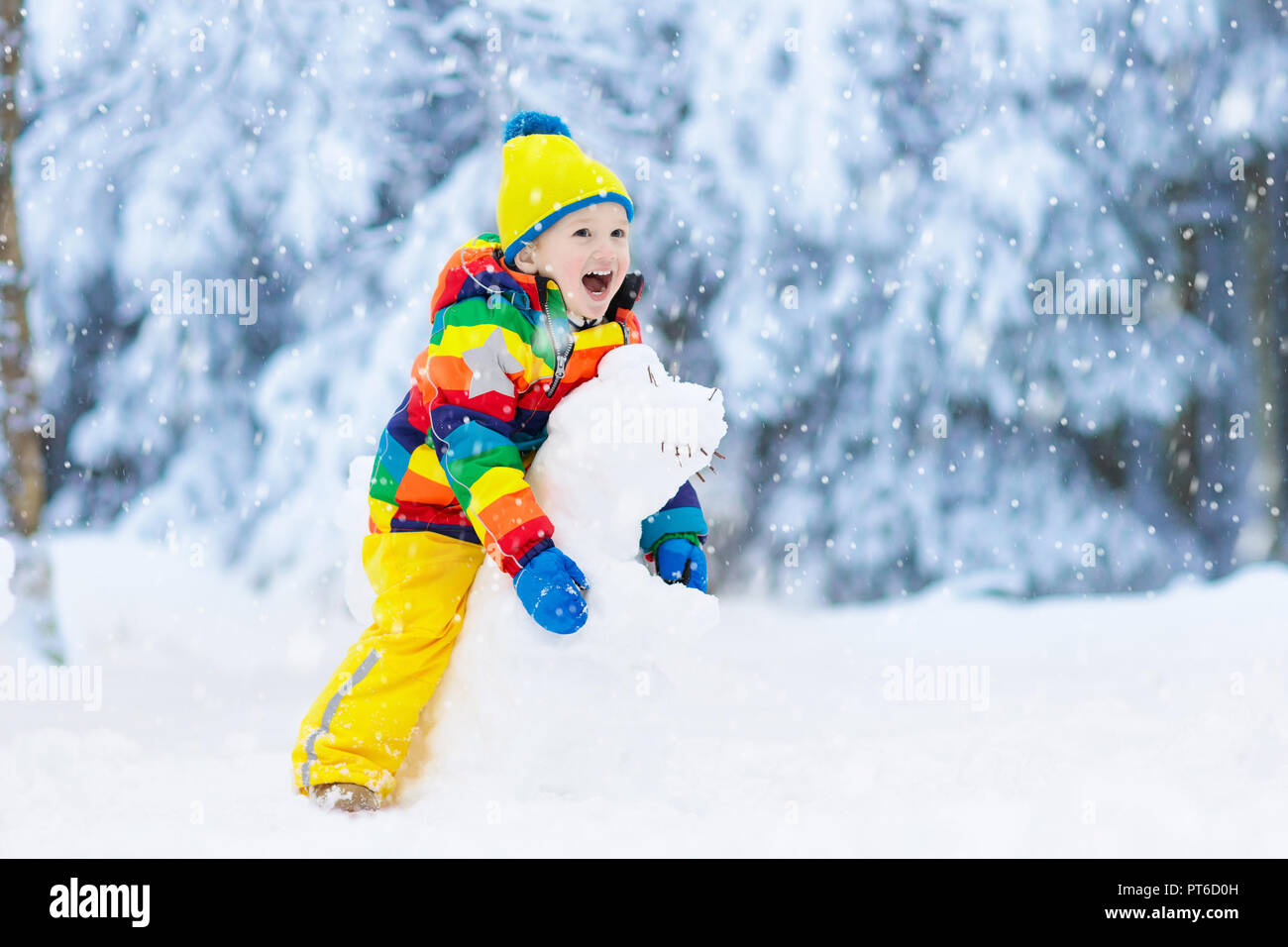 Kid making snowman in snowy winter park. Children play in snow. Baby ...