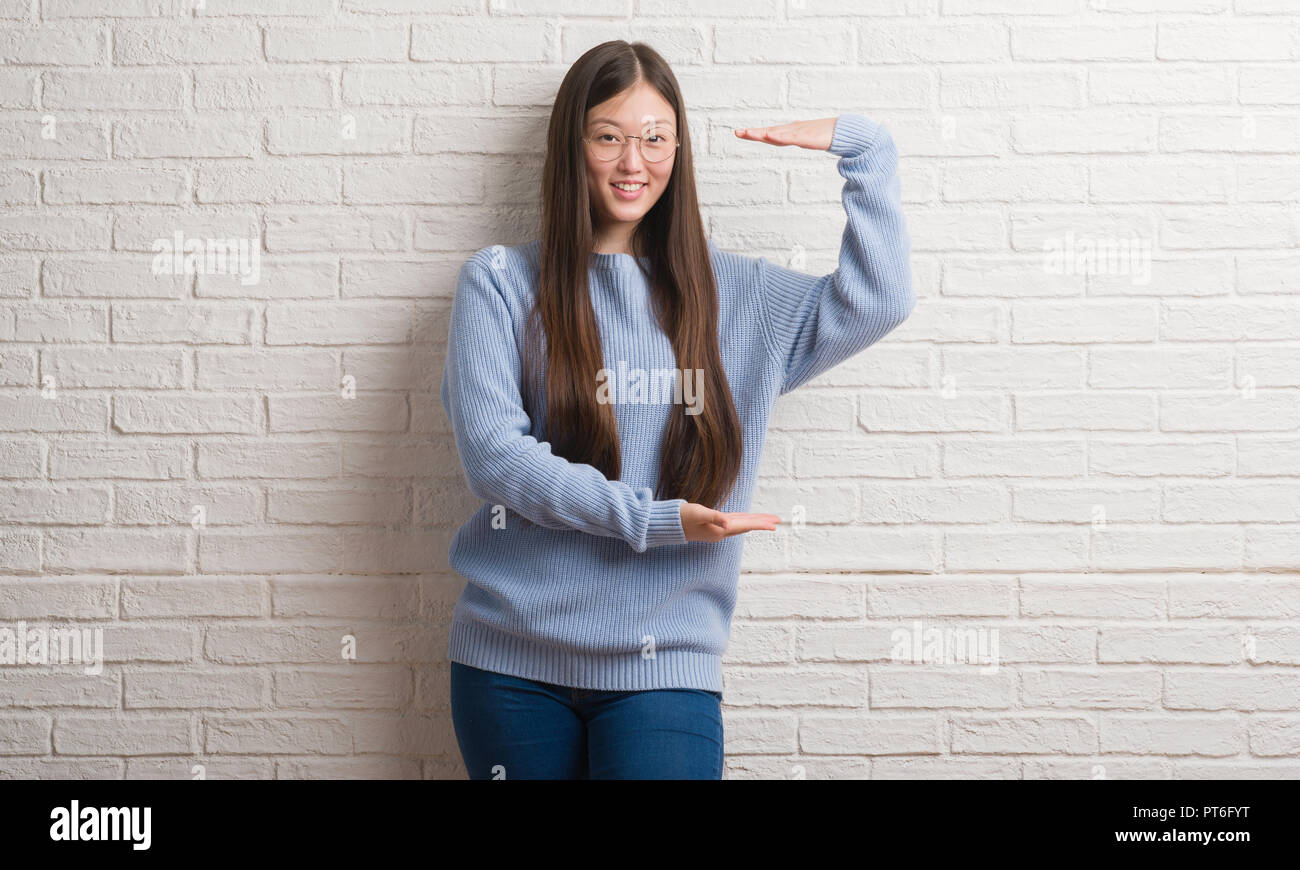 Young Chinise woman over white brick wall gesturing with hands showing ...