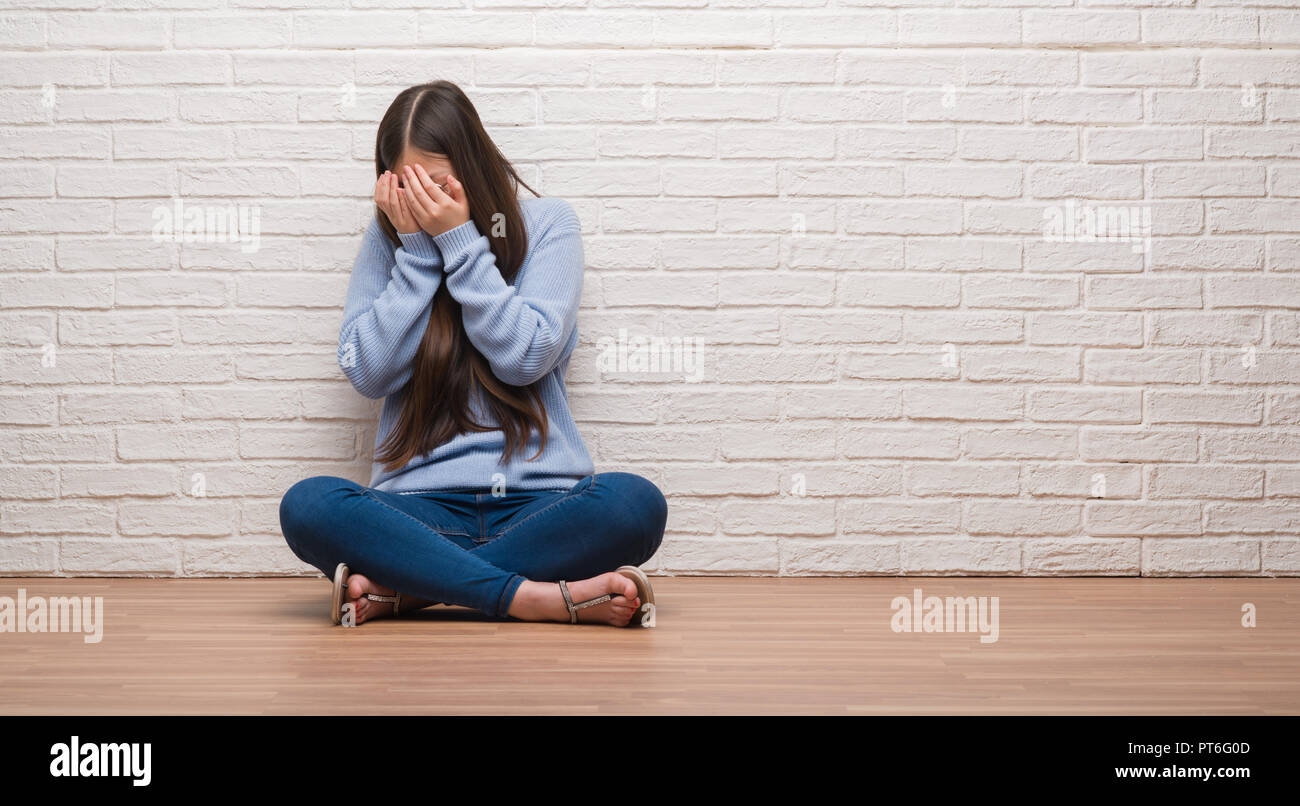 Young Chinese woman sitting on the floor over brick wall with sad ...