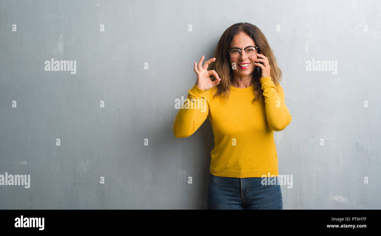 Middle age hispanic woman talking on the phone doing ok sign with ...