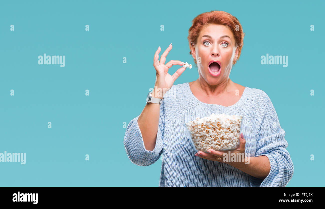 Atrractive senior caucasian redhead woman eating popcorn over isolated ...