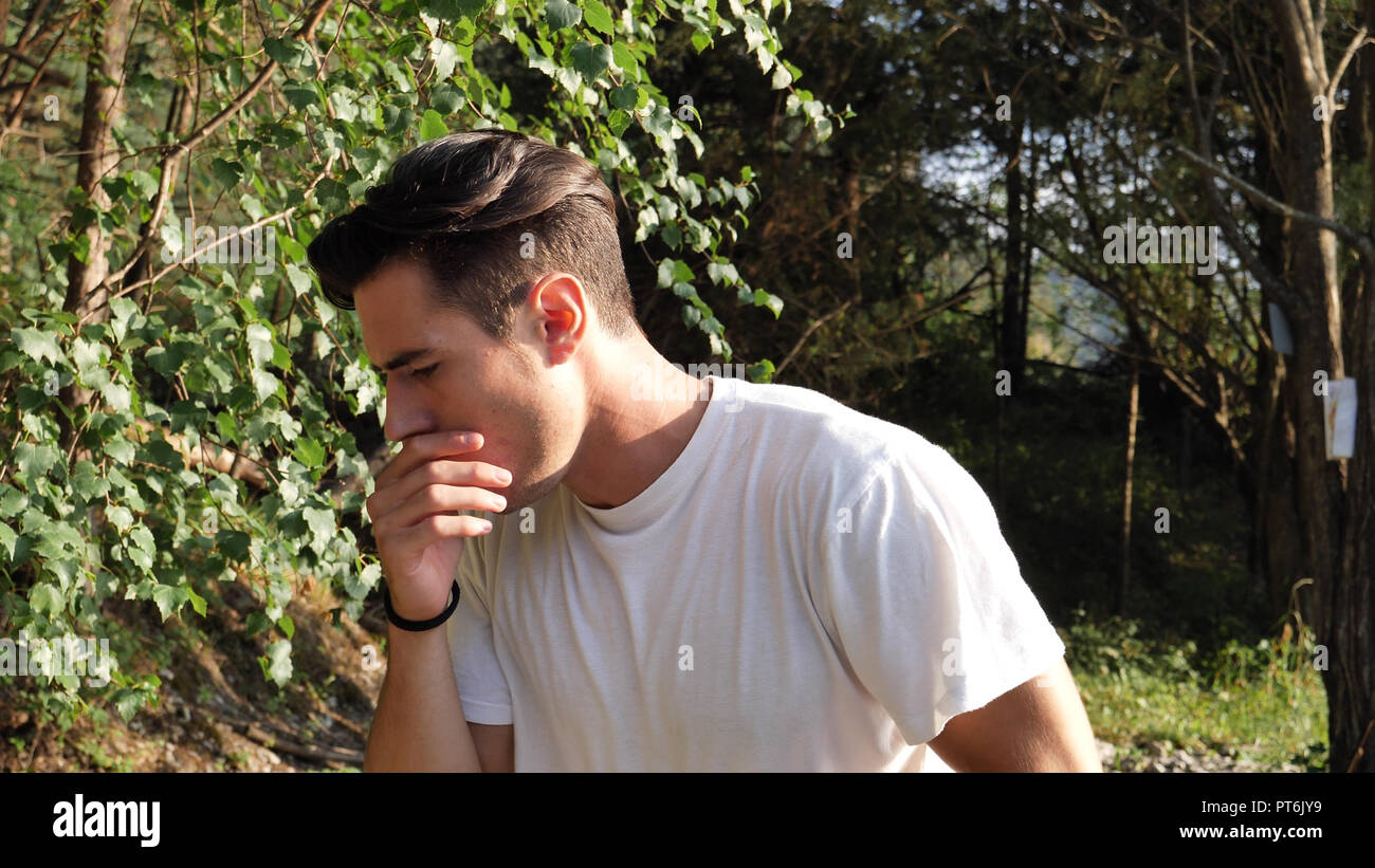 Young man coughing in nature in white t-shirt Stock Photo - Alamy