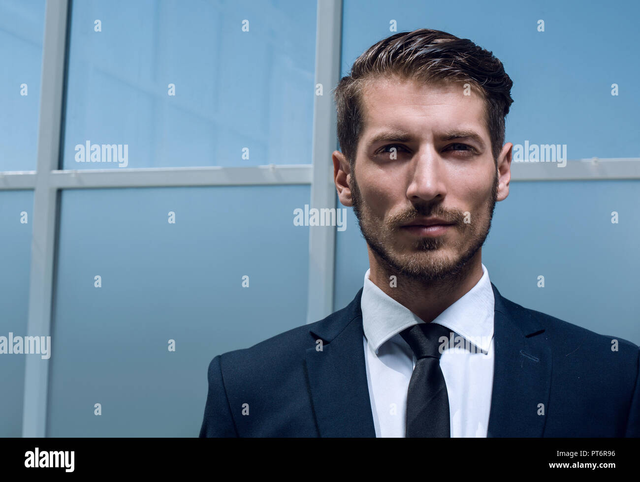 young successful businessman with a serious face stands in the office ...
