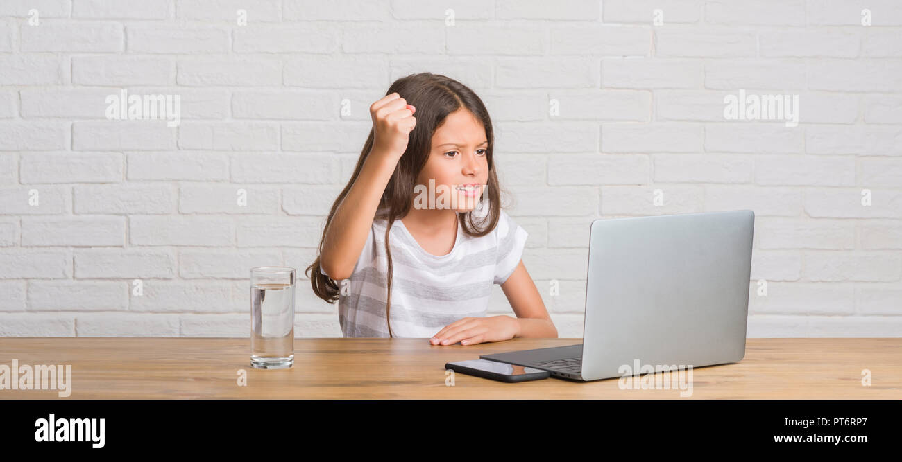 Young hispanic kid sitting on the table using computer laptop annoyed ...