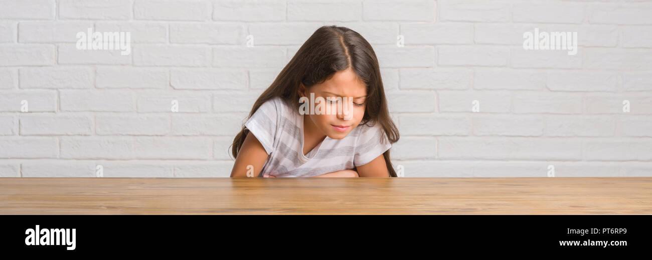 Young hispanic kid sitting on the table at home with hand on stomach ...