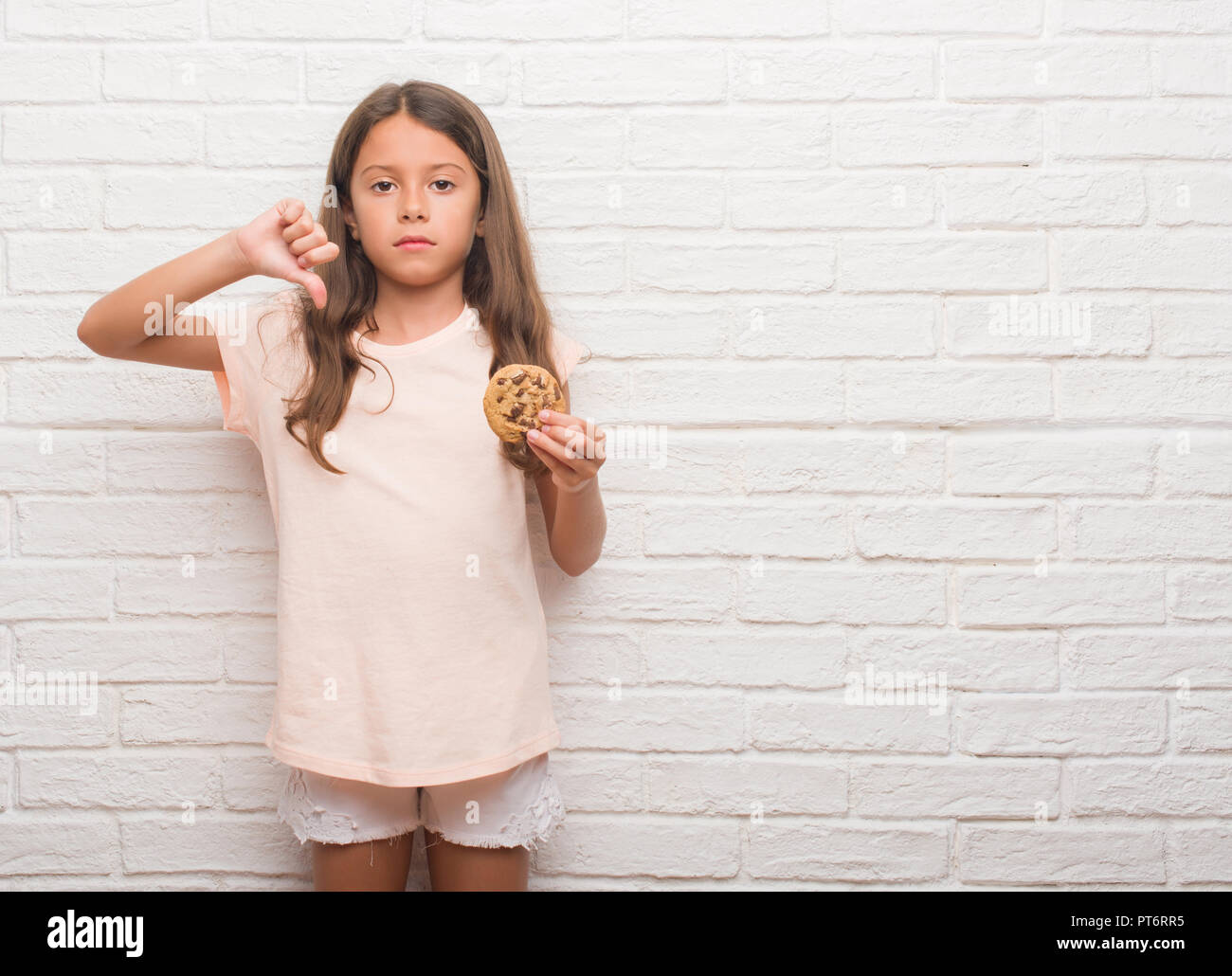 Young hispanic kid over white brick wall eating chocolate chips cooky ...