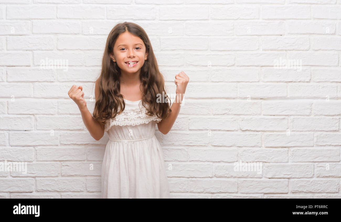 Young hispanic kid over white brick wall celebrating surprised and ...