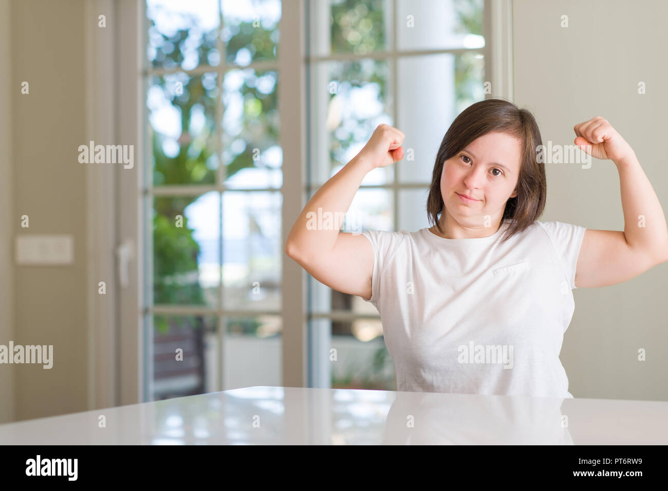 Down syndrome woman at home showing arms muscles smiling proud. Fitness ...