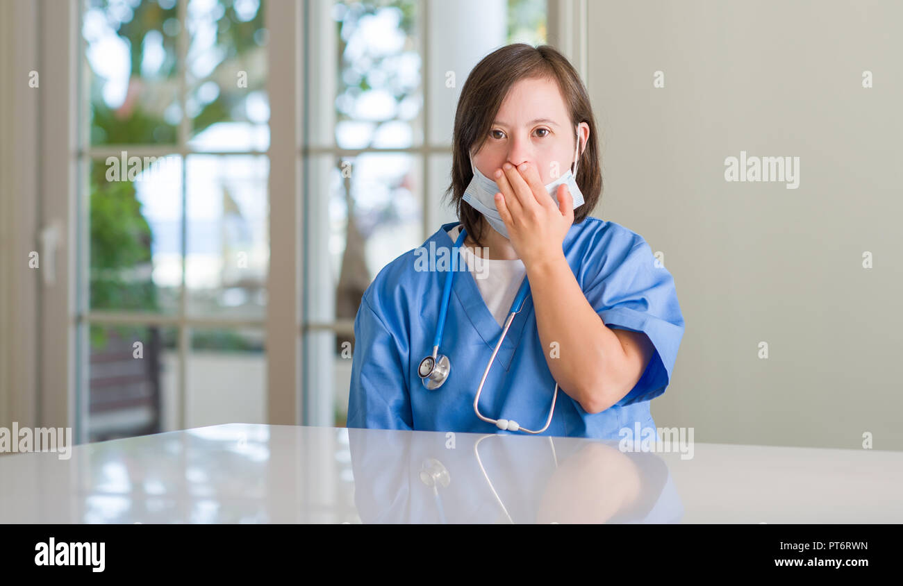 Down syndrome woman wearing nurse uniform cover mouth with hand shocked ...