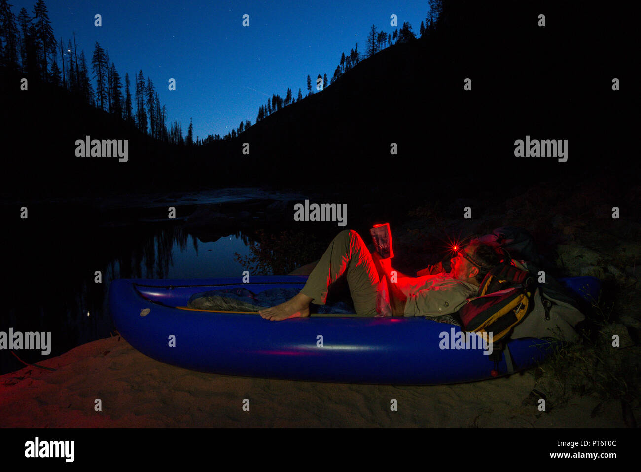 Reading a book at night laying in an inflatable kayak at a campsite on ...