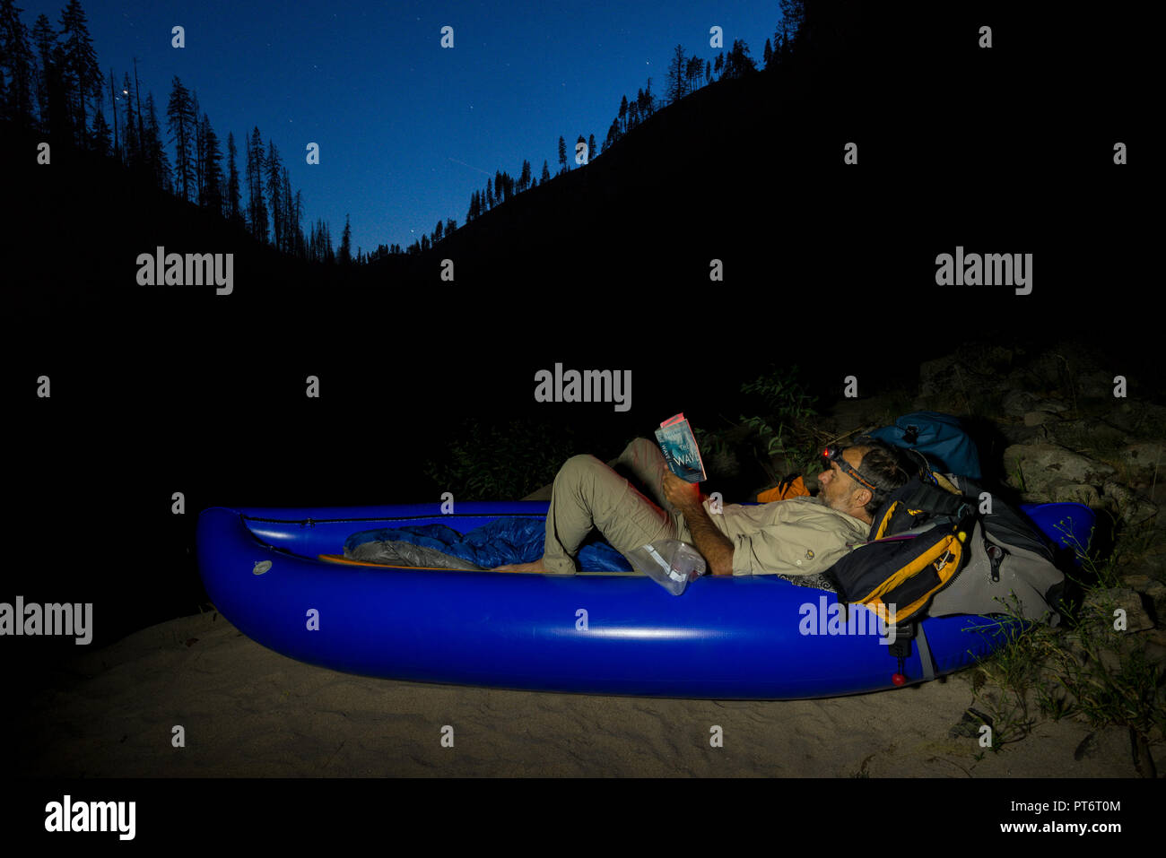 Reading a book at night laying in an inflatable kayak at a campsite on ...