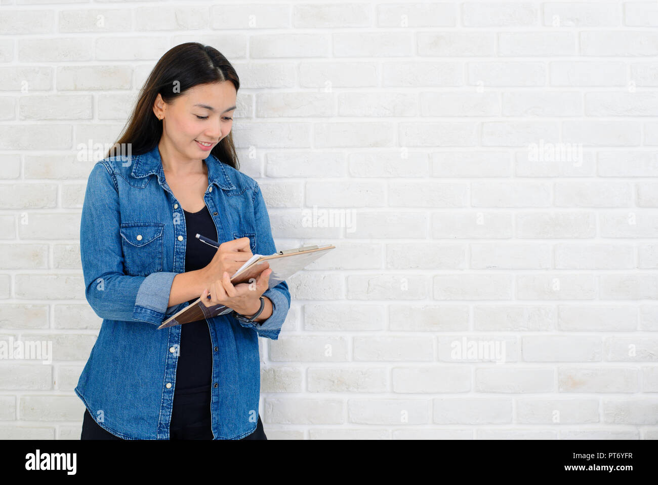 Asian woman holding a notebook and a pen ready to take notes standing ...