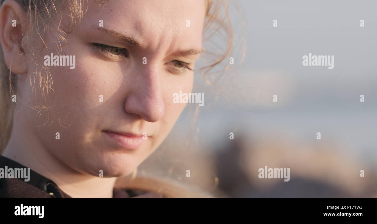 young female closeup portrait sitting on a seashore with thoughtful ...