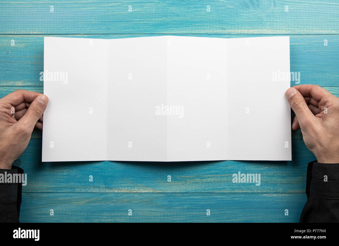 Mens hands holding empty white booklet on blue wooden background. View ...