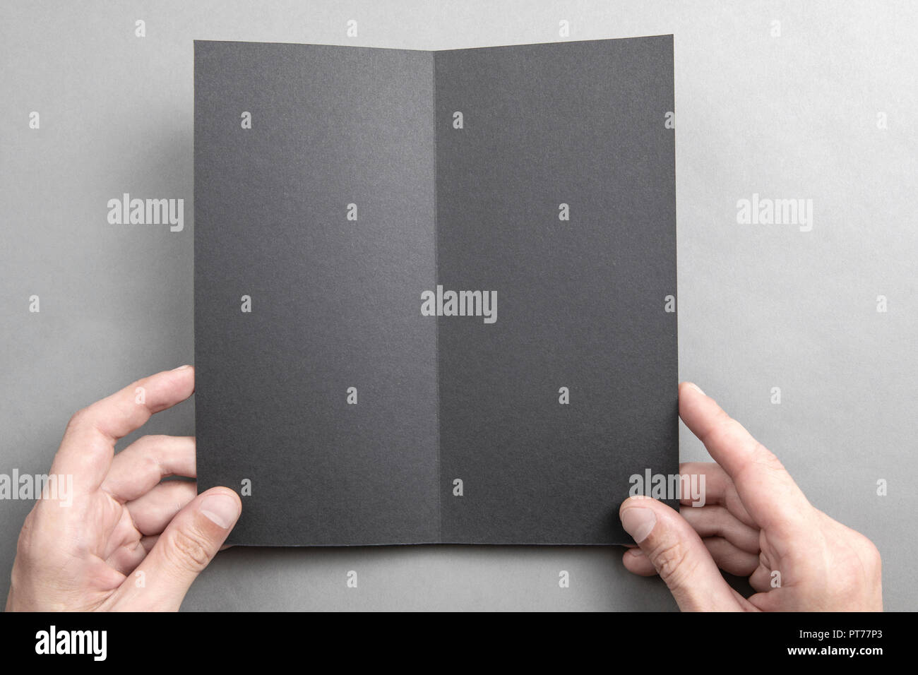 Mens hands holding empty black booklet on gray background. View from ...