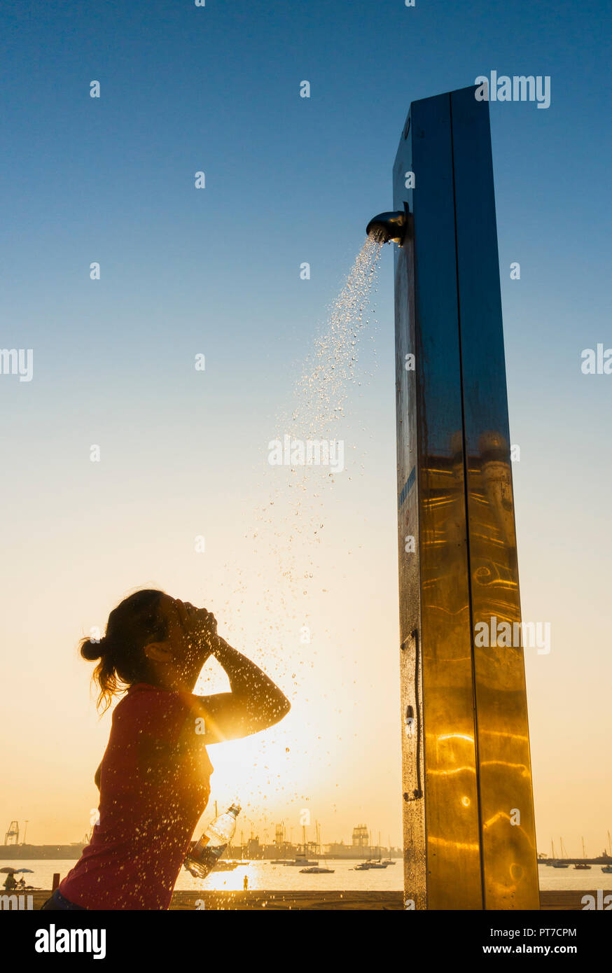 Female jogger cooling down under beach shower at sunrise during ...