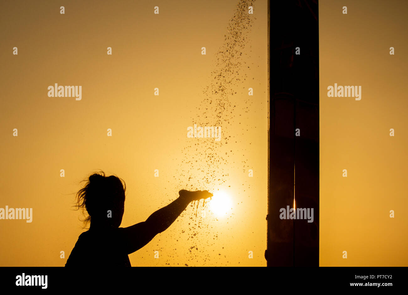 Female jogger cooling down under beach shower at sunrise during ...