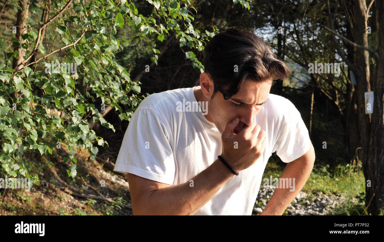 Young man coughing in nature in white t-shirt Stock Photo - Alamy