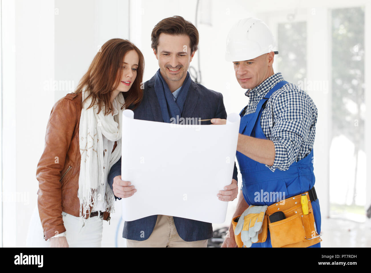Worker shows house design plans to a young couple at construction site ...