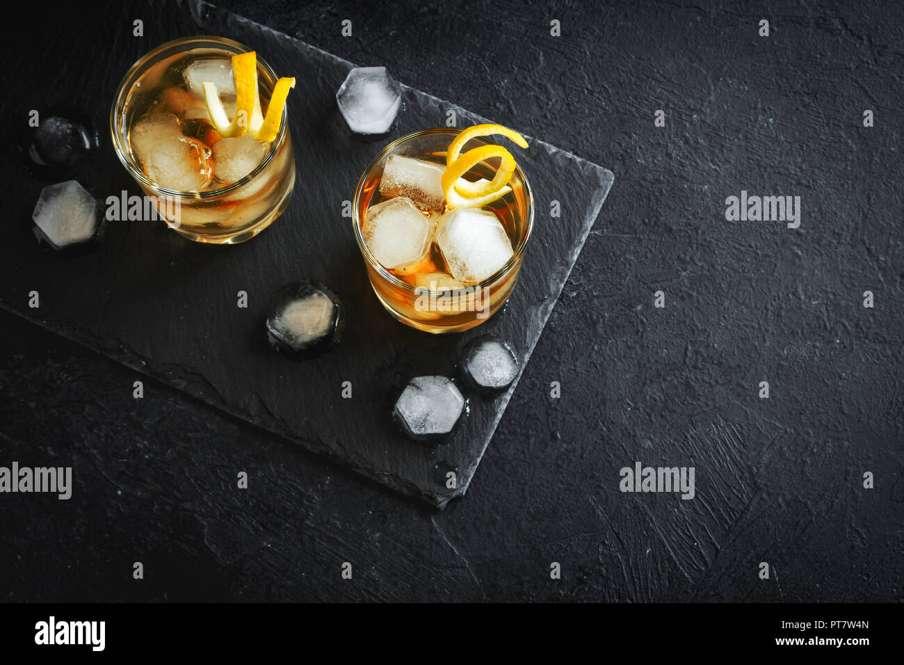 Whiskey or Rum on rocks with lemon twist on black stone background, top ...