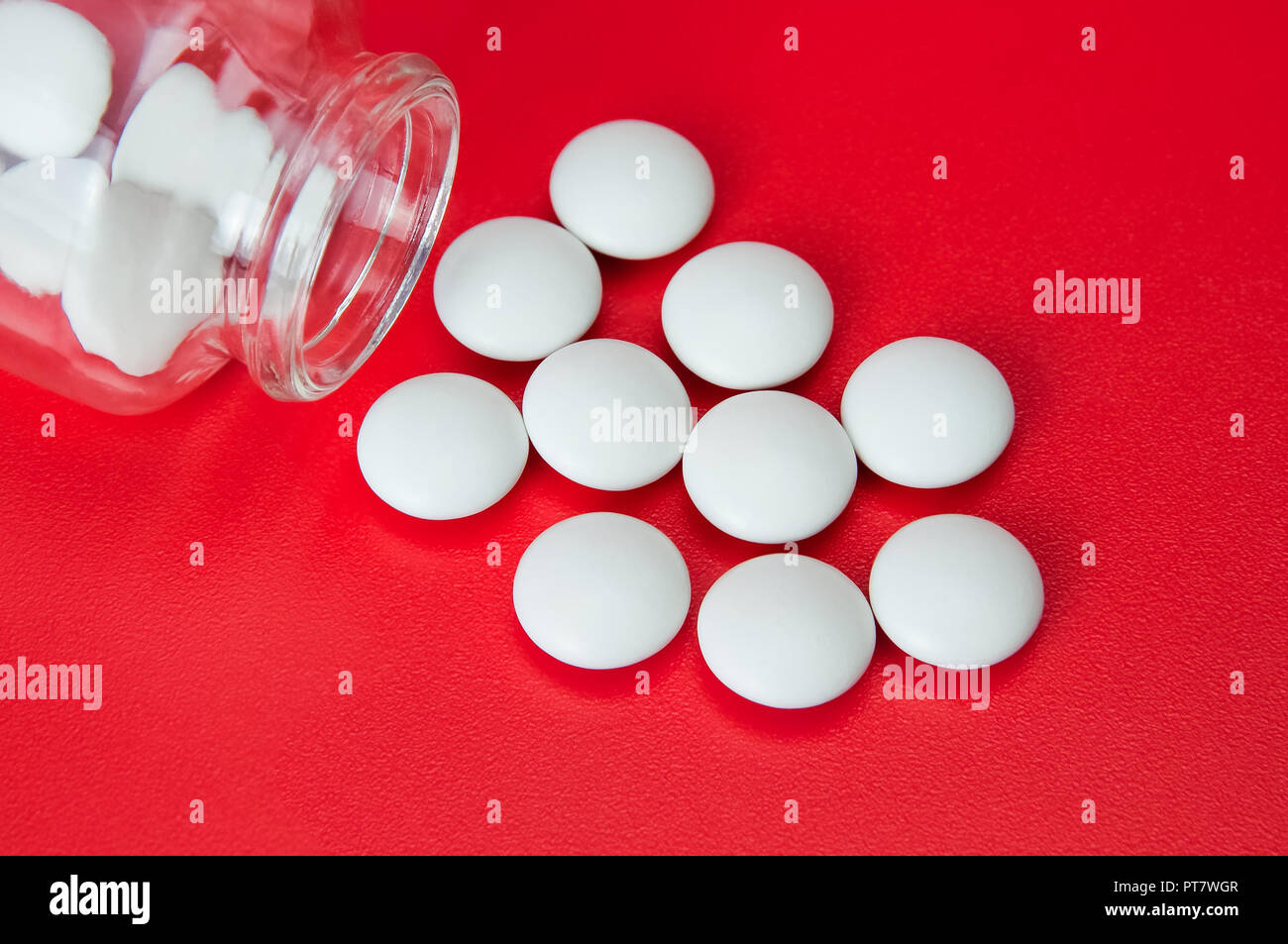 White tablets are scattered from a glass bottle on a red background ...