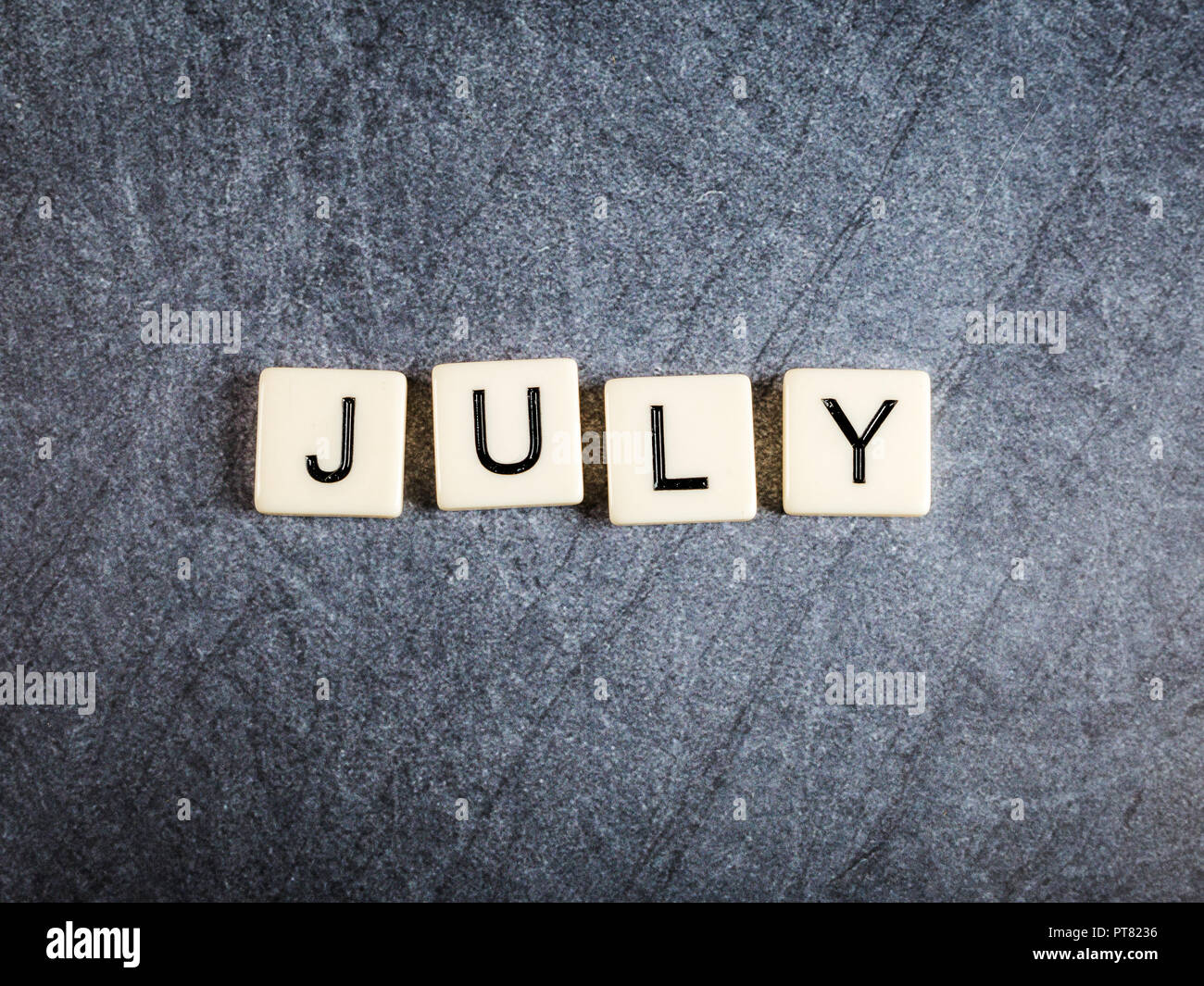 Letter tiles on black slate background spelling July Stock Photo - Alamy