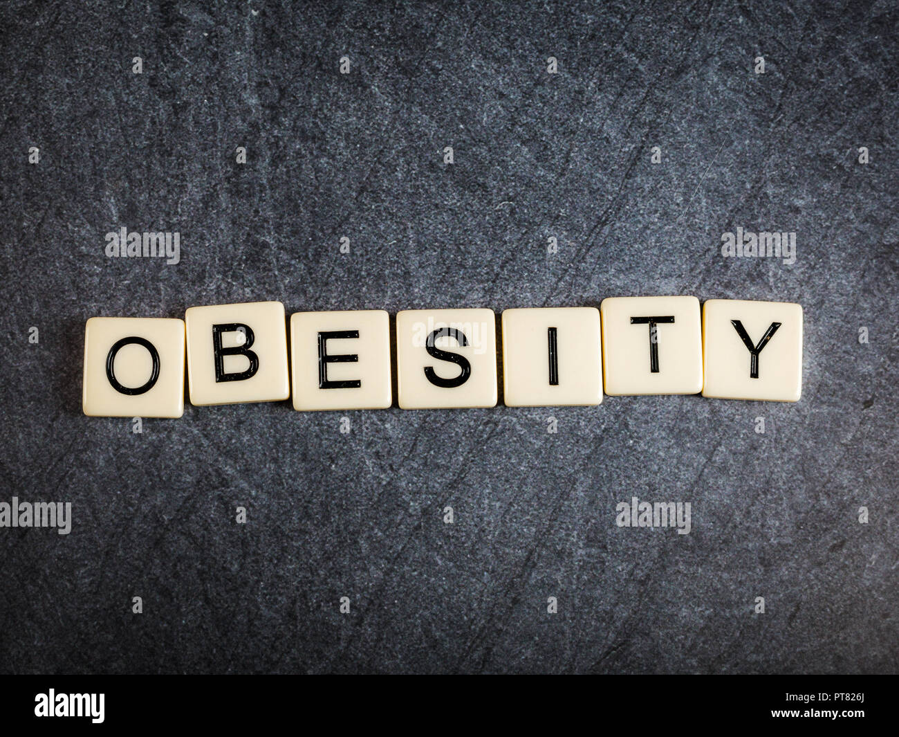 Letter tiles on black slate background spelling Obesity Stock Photo - Alamy