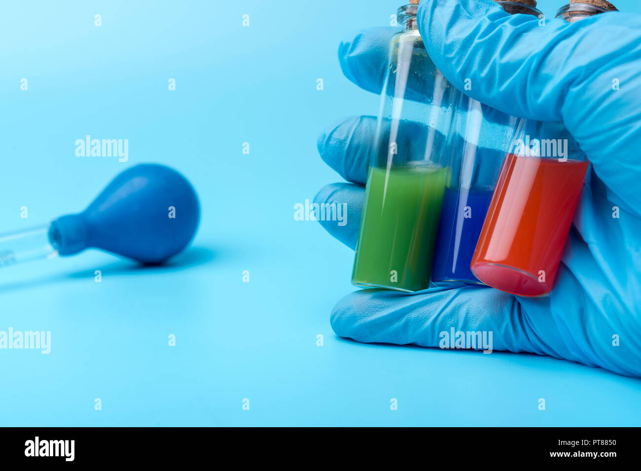 A gloved hand holds three vials of different liquid inside on a blue ...