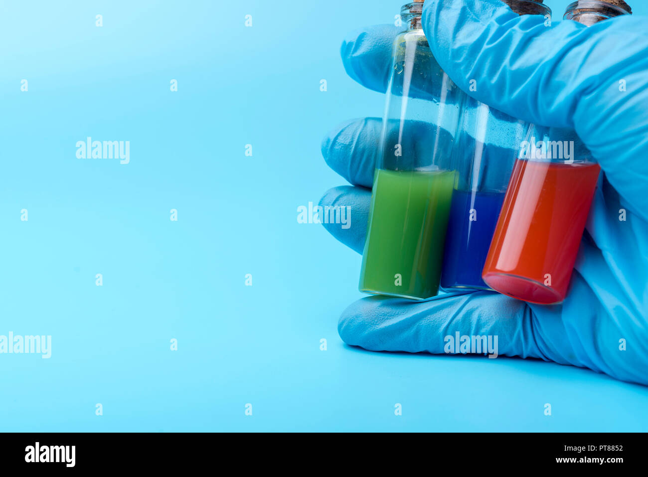 A gloved hand holds three vials of different liquid inside on a blue ...