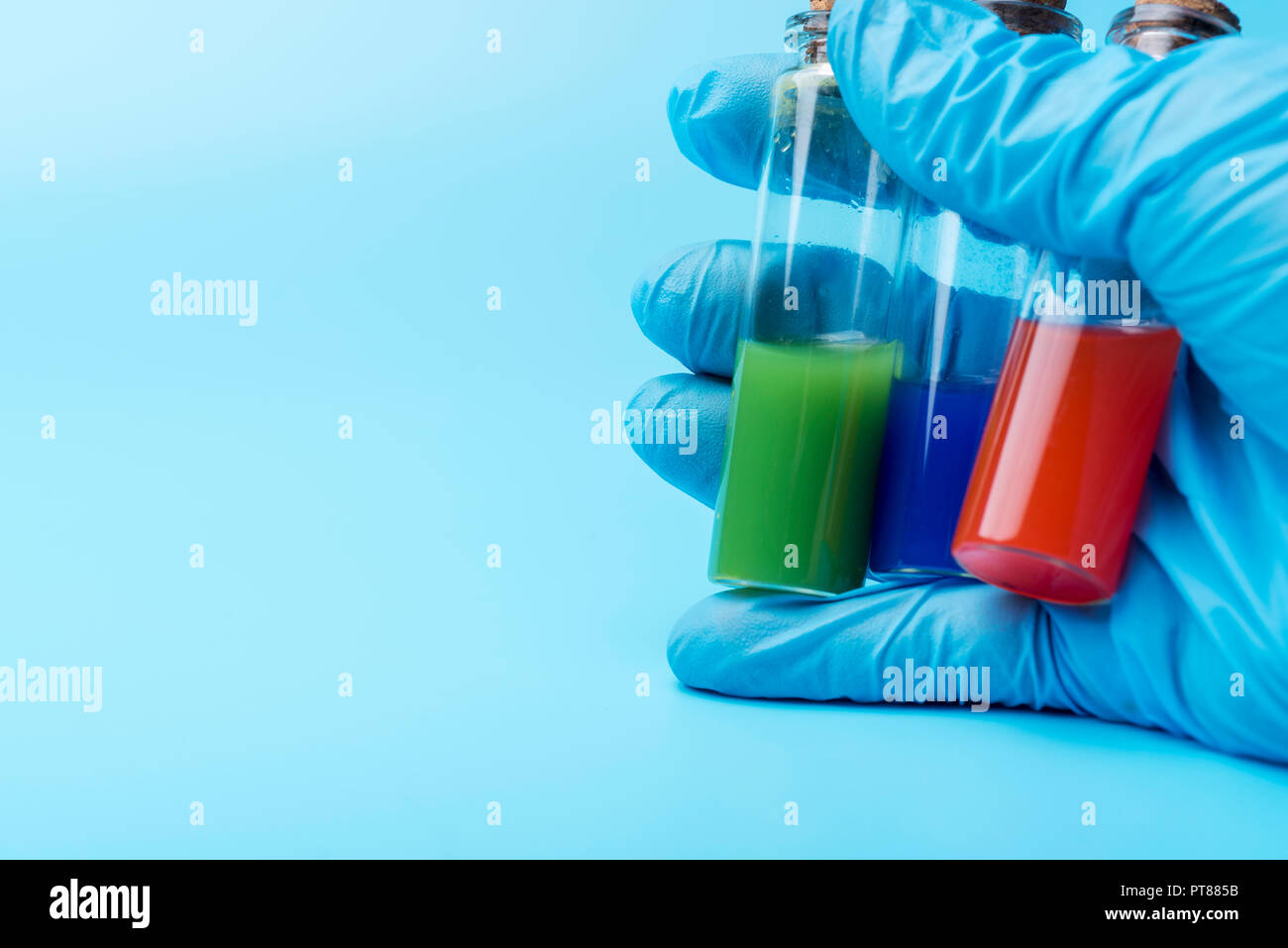 A gloved hand holds three vials of different liquid inside on a blue ...