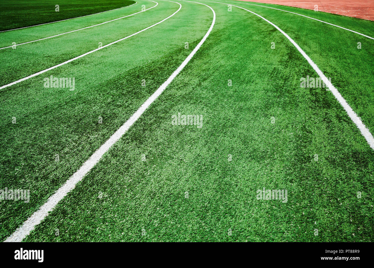 Empty running track with bright green artificial turf and white lines ...